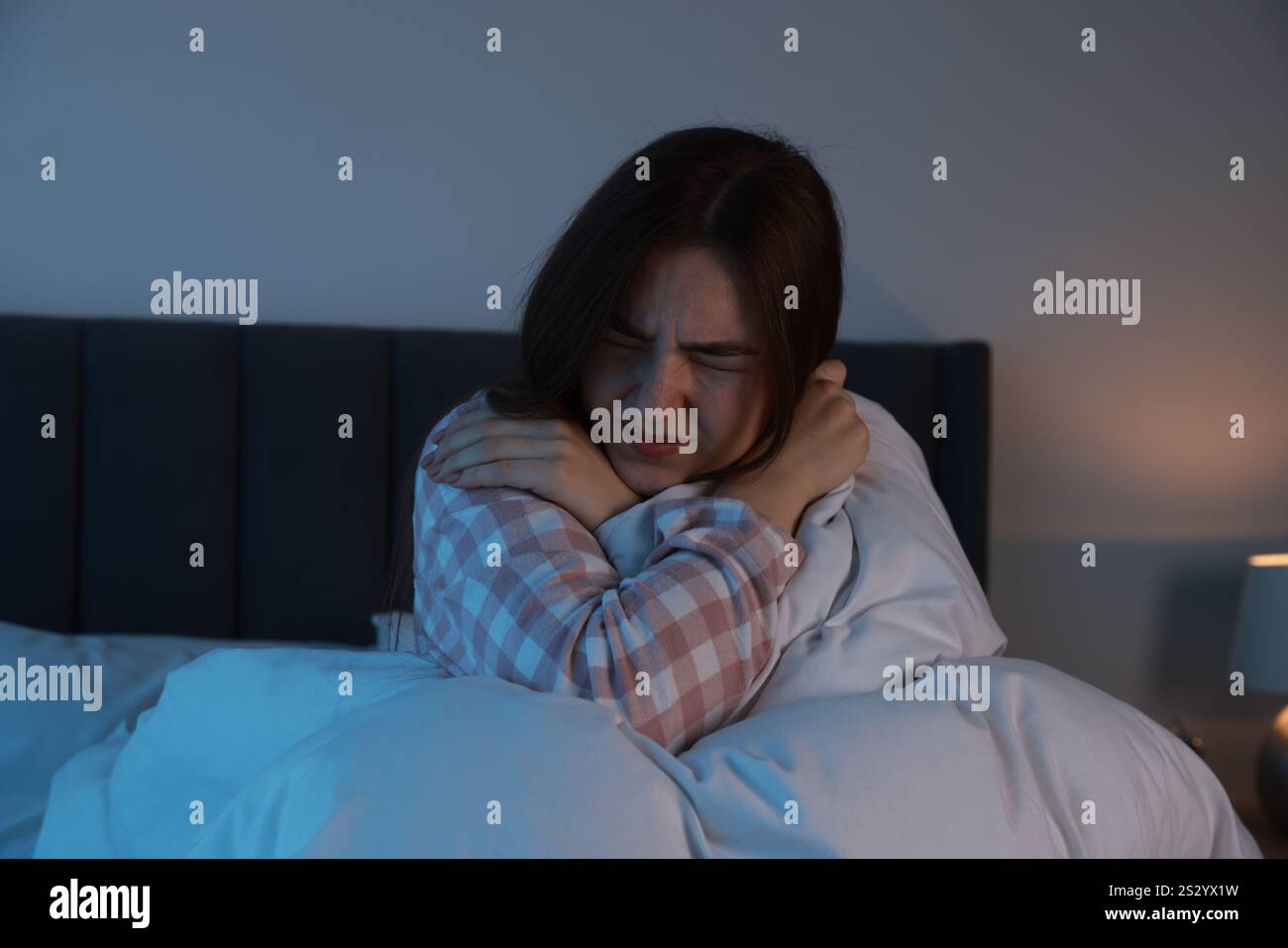 Fear of darkness. Scared young woman lying on bed in room at night ...