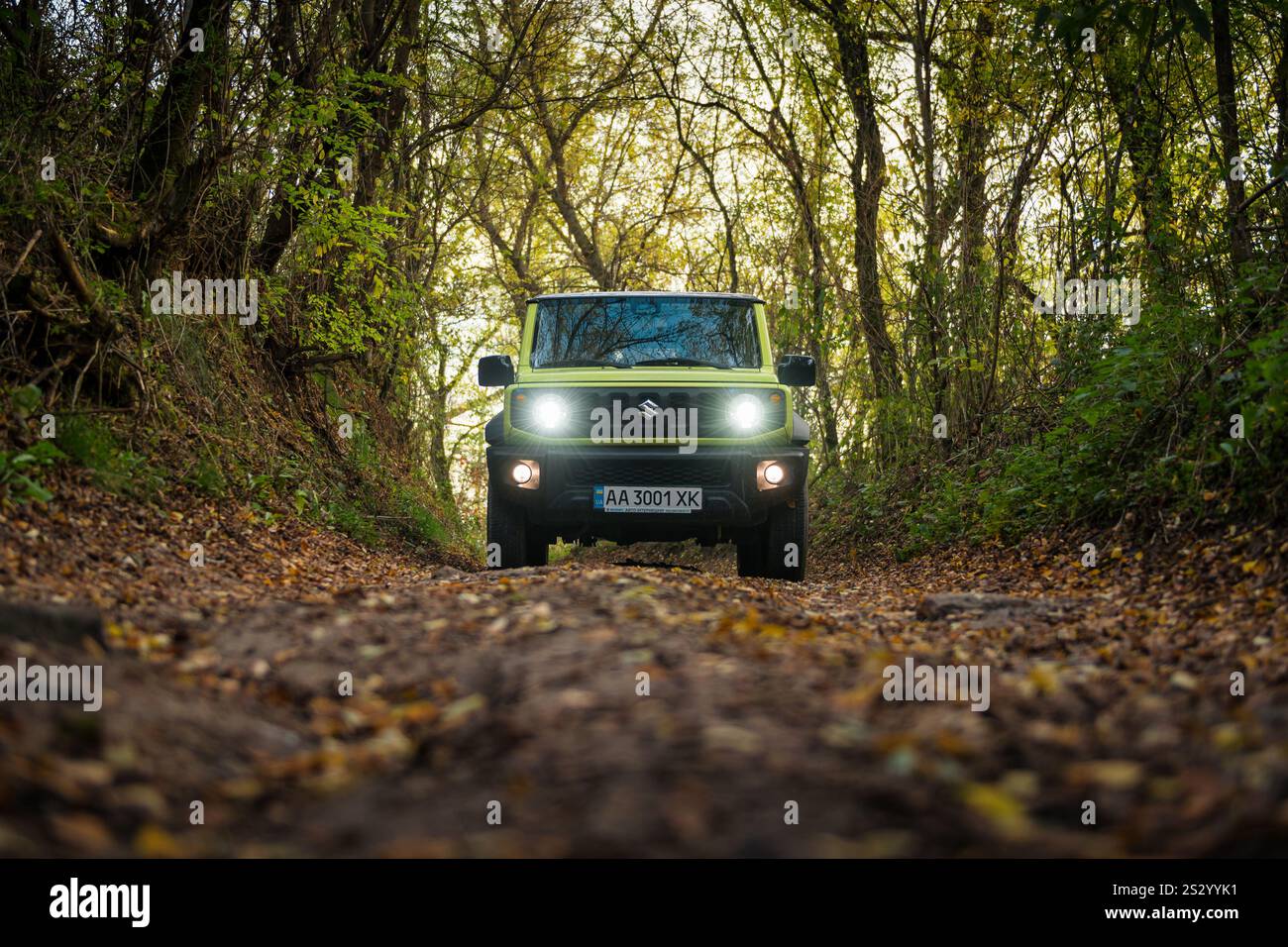 Lime green Suzuki Jimny in autumn forest. Front view of mini SUV on ...