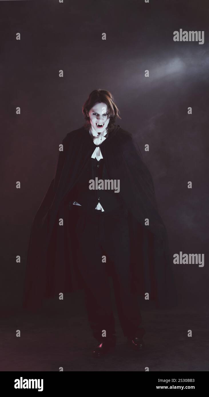 Man in black suit and cape, as vampire, faces forward, displaying fangs ...