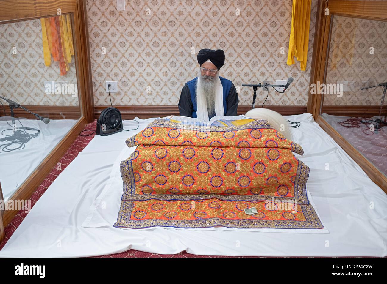 A Sikh priest reads from the holy book Guru Granth Sahib in a glass ...