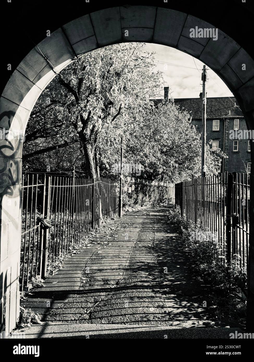 A black-and-white view of a path leading through an arched stone ...
