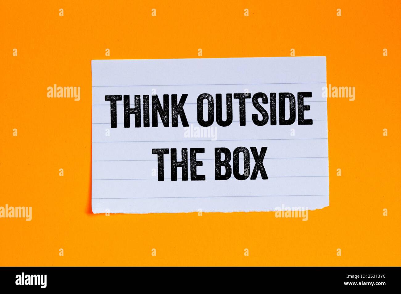 Think outside the box message written on ripped torn white paper piece on orange background ...