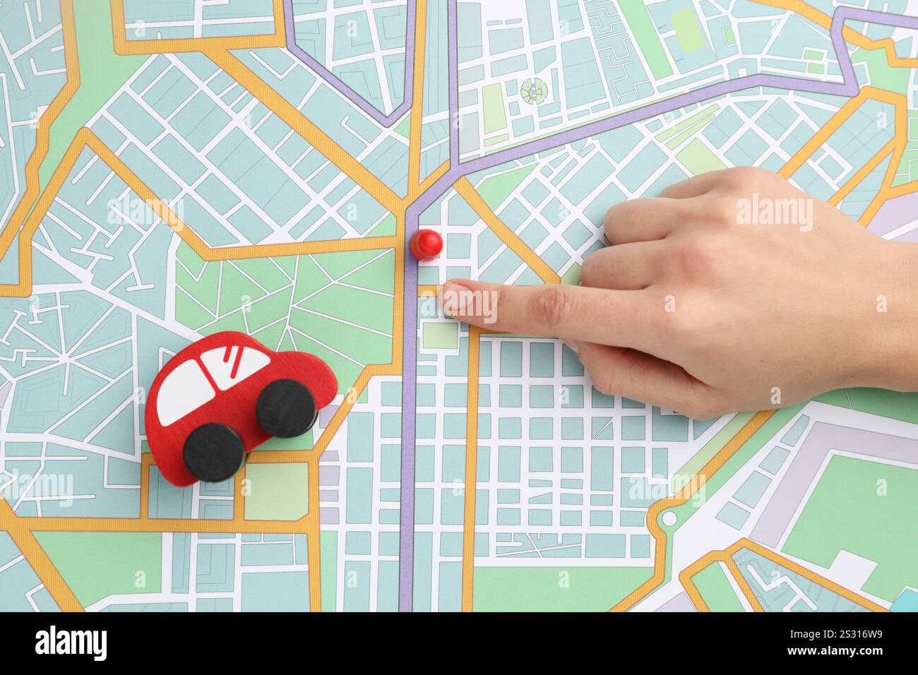 Woman pointing at city map near human figure and toy car, top view ...