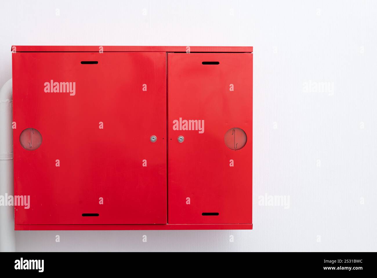 A bright red metal cabinet is isolated on a white wall background. The ...