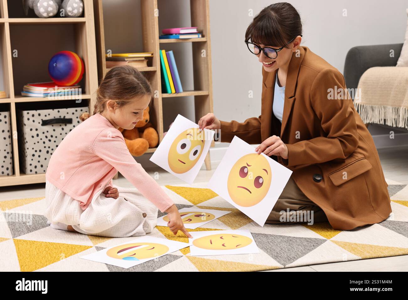 Autism therapy. Little girl choosing emoticon with smiling psychologist ...