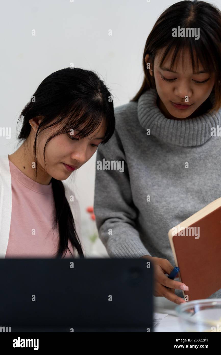 Female higher education student using laptop and studying book in home ...
