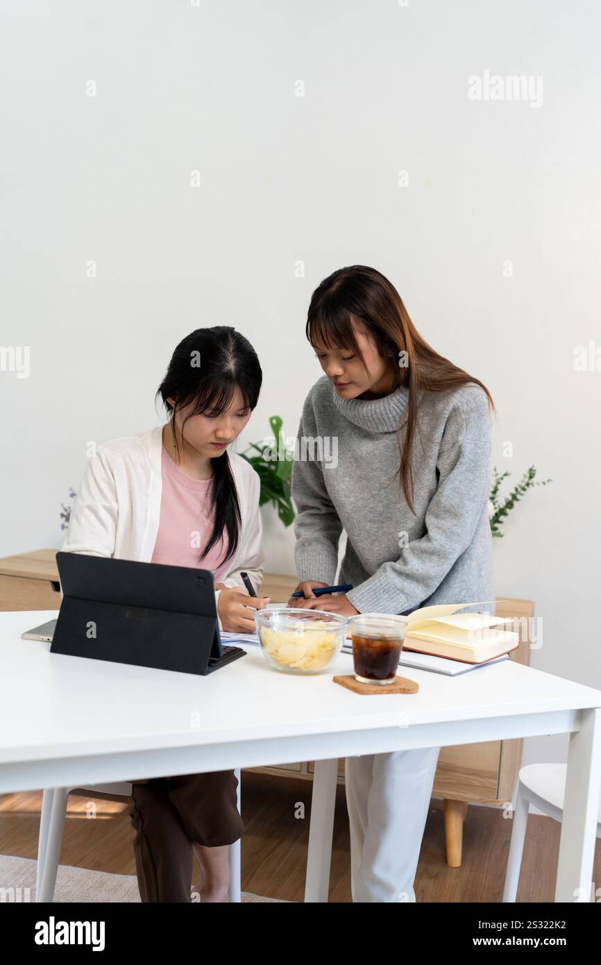 Female higher education student using laptop and studying book in home ...