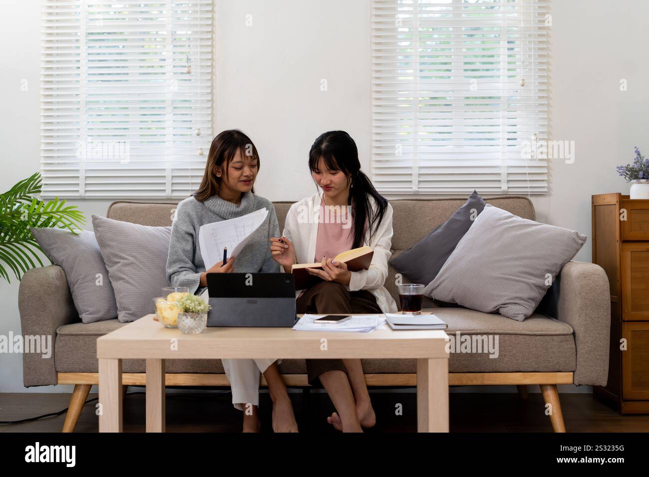 Female higher education student using laptop and studying book in home ...