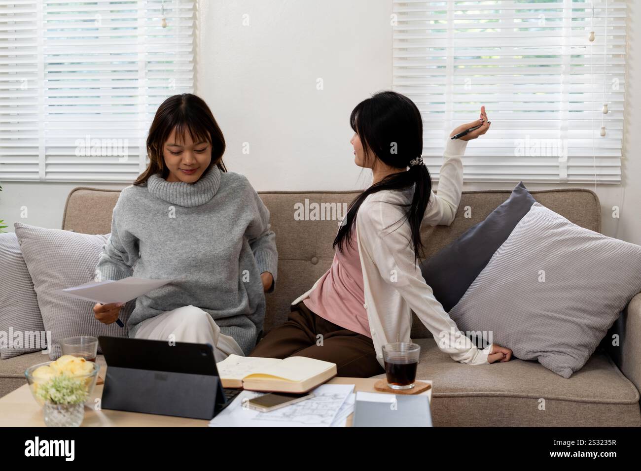 Female higher education student using laptop and studying book in home ...