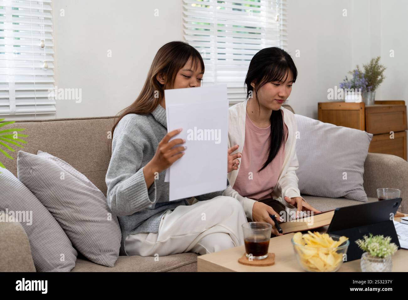 Female higher education student using laptop and studying book in home ...