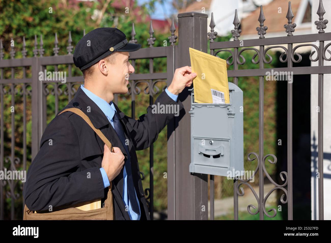 Happy postman putting envelope into mail box outdoors Stock Photo - Alamy