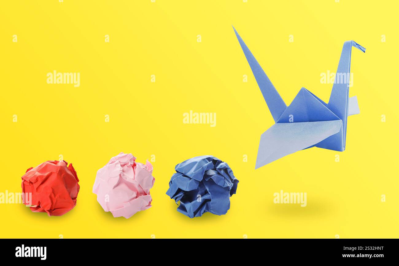 Blue origami crane and crumpled paper balls on yellow background ...