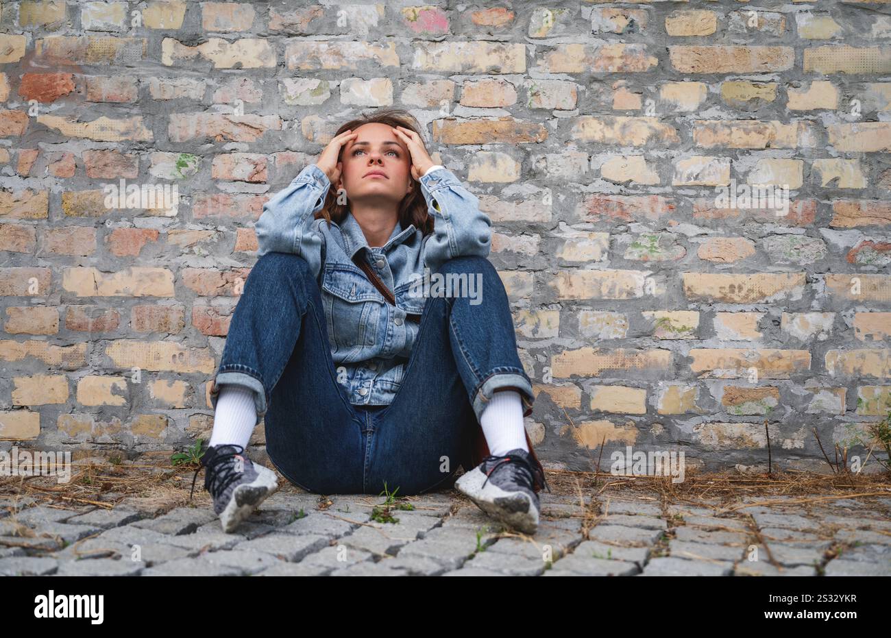 Urban stressed woman sitting next to brick wall outdoors in city street ...