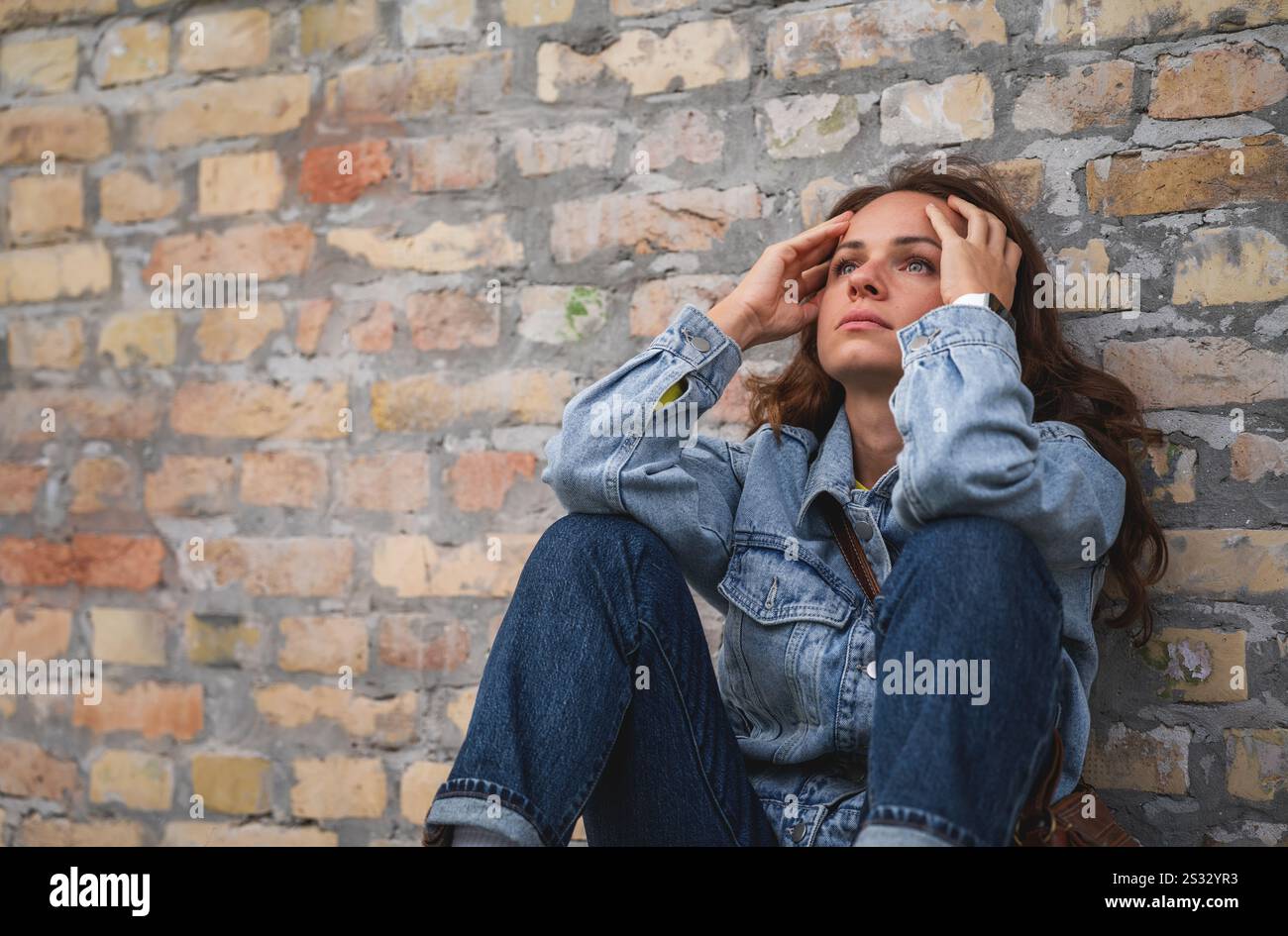 Urban stressed woman sitting next to brick wall outdoors in city street ...