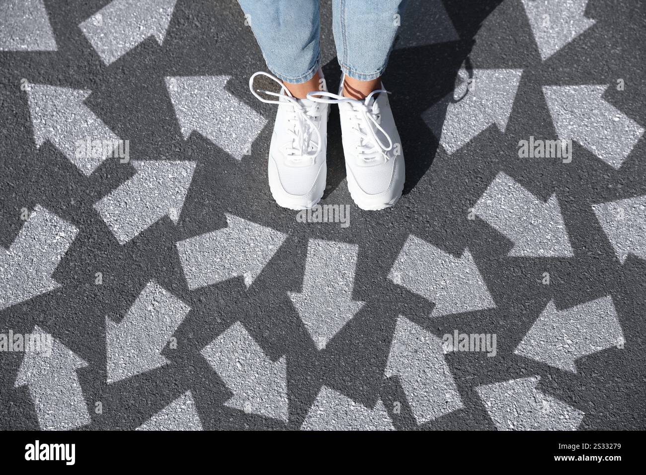 Woman standing on asphalt road with white arrows pointing in different ...