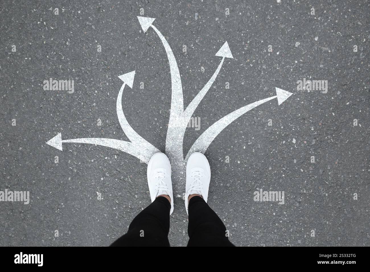 Woman standing on asphalt road with white arrows pointing in different ...