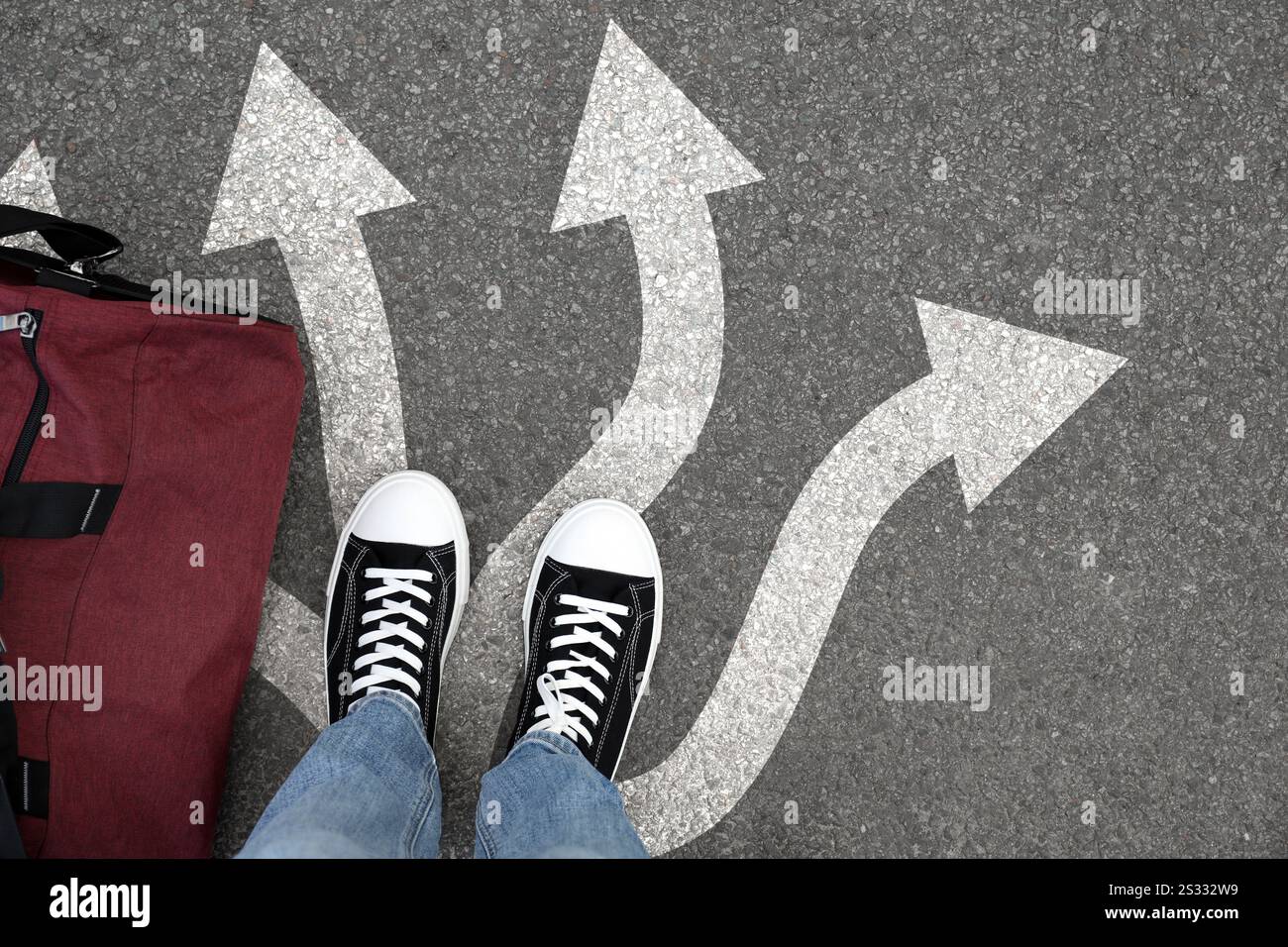 Man standing on asphalt road with white arrows pointing in different ...