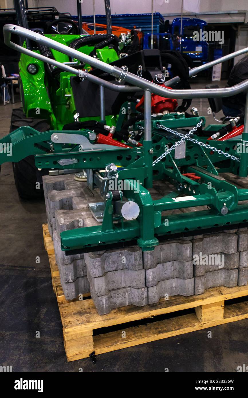 A green mechanical grab lifting a pallet of gray concrete paving stones ...