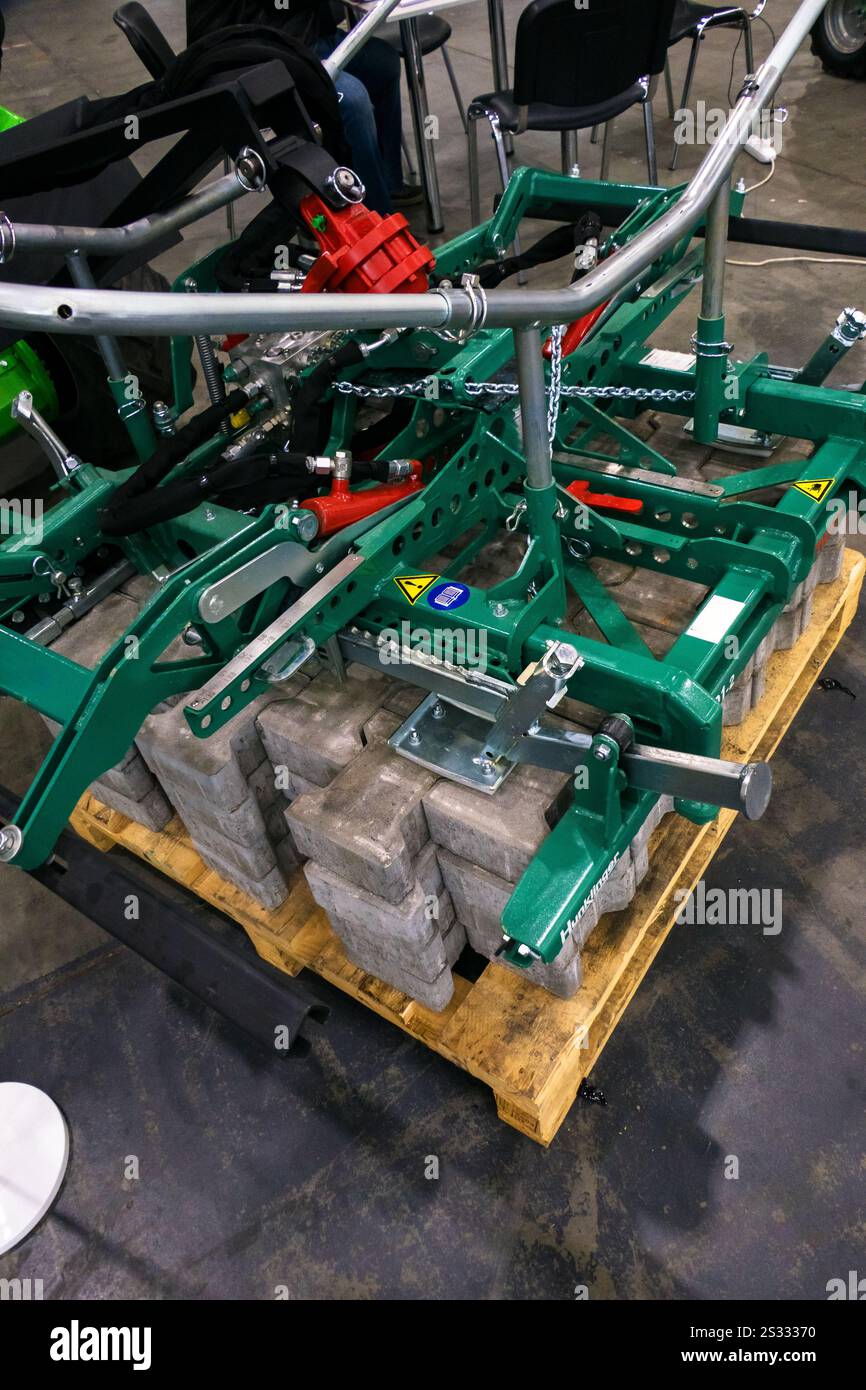 A green mechanical grab lifting a pallet of gray concrete paving stones ...