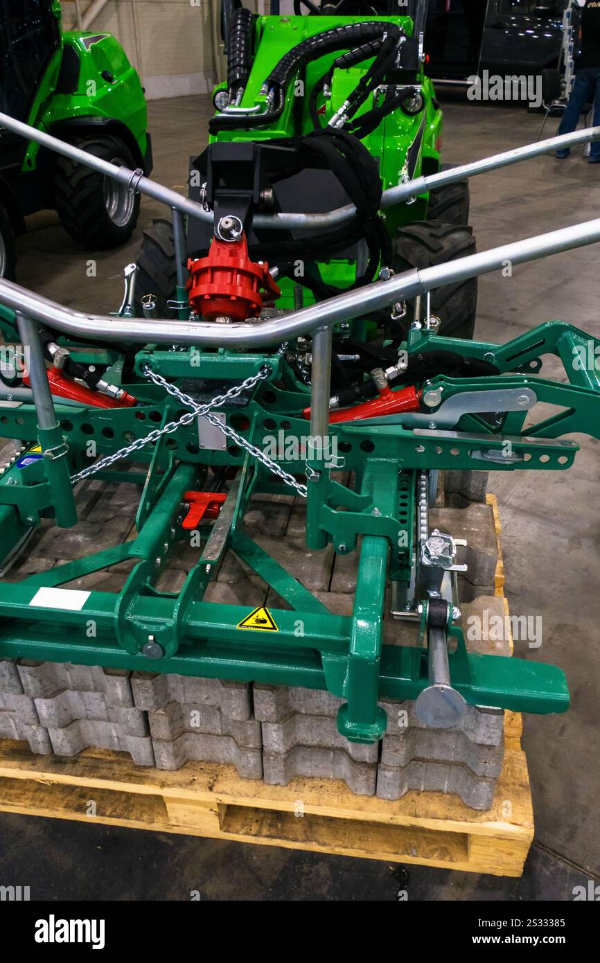 A green mechanical grab lifting a pallet of gray concrete paving stones ...