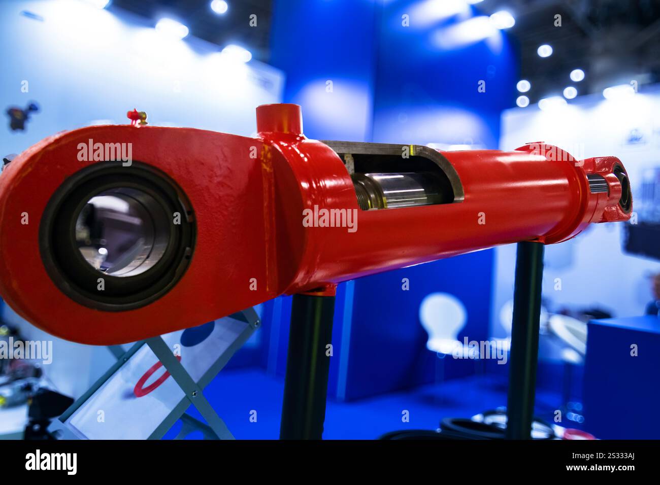 The image shows a large red hydraulic cylinder. The cylinder is mounted ...