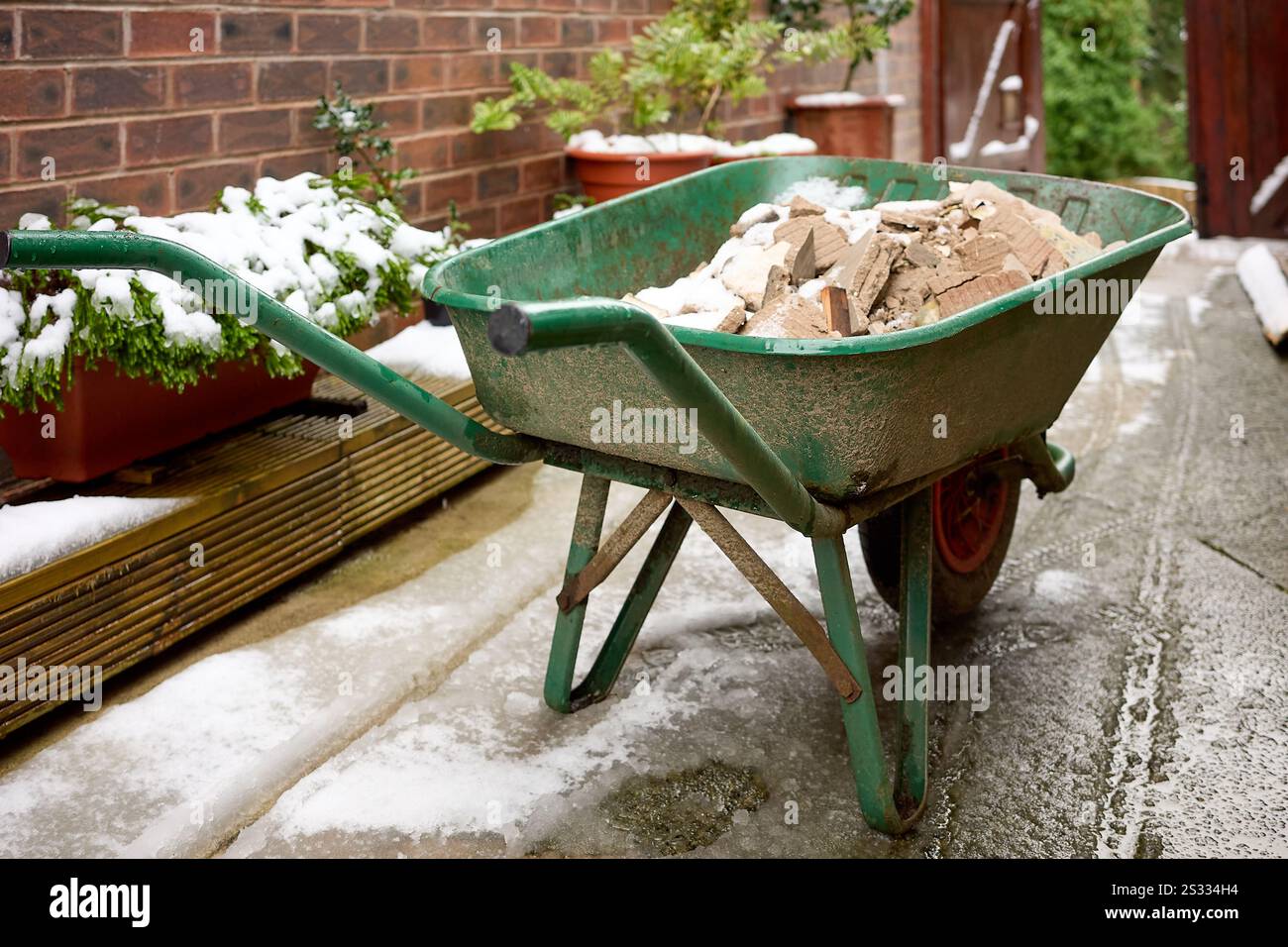 Green wheelbarrow filled with bricks plaster and cement on a snowy ...