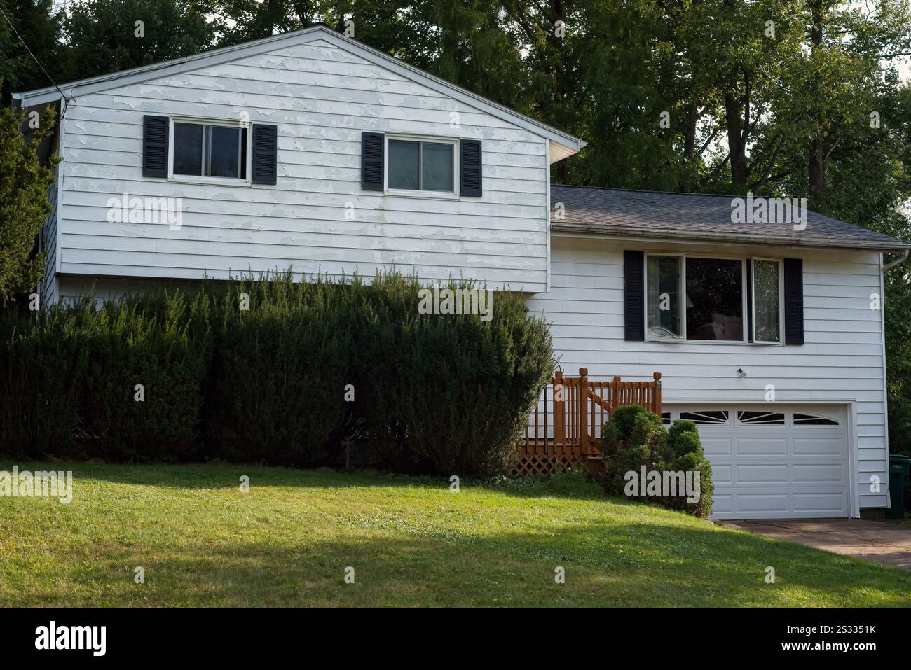 A split-level house with peeling paint on the aluminum siding and ...