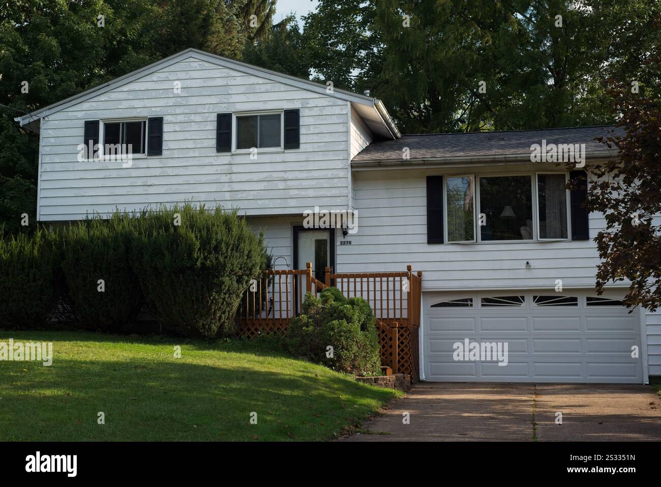 A split-level house with peeling paint on the aluminum siding and ...