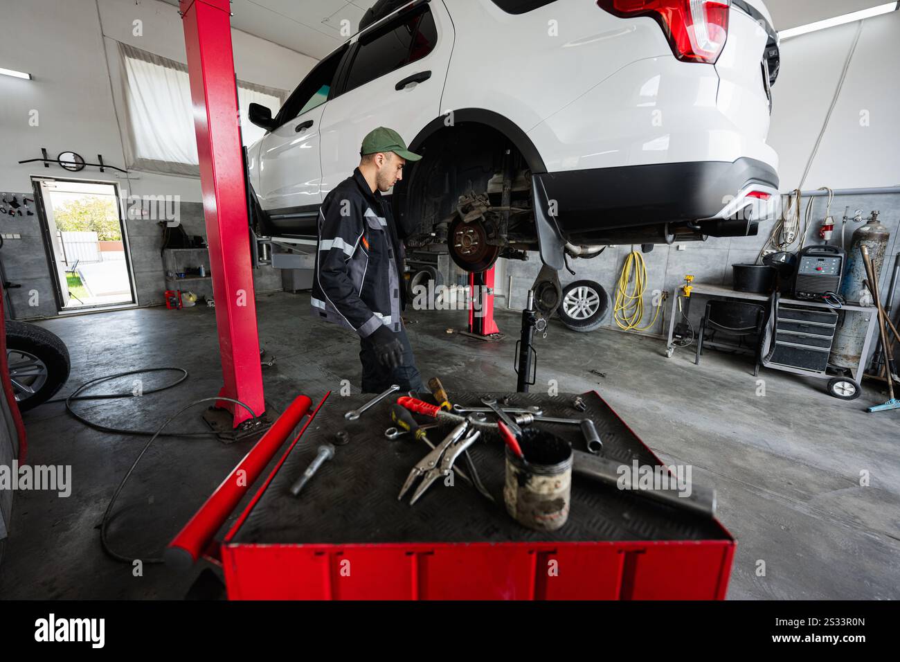 A mechanic wearing workwear inspects an SUV lifted on a hydraulic ...