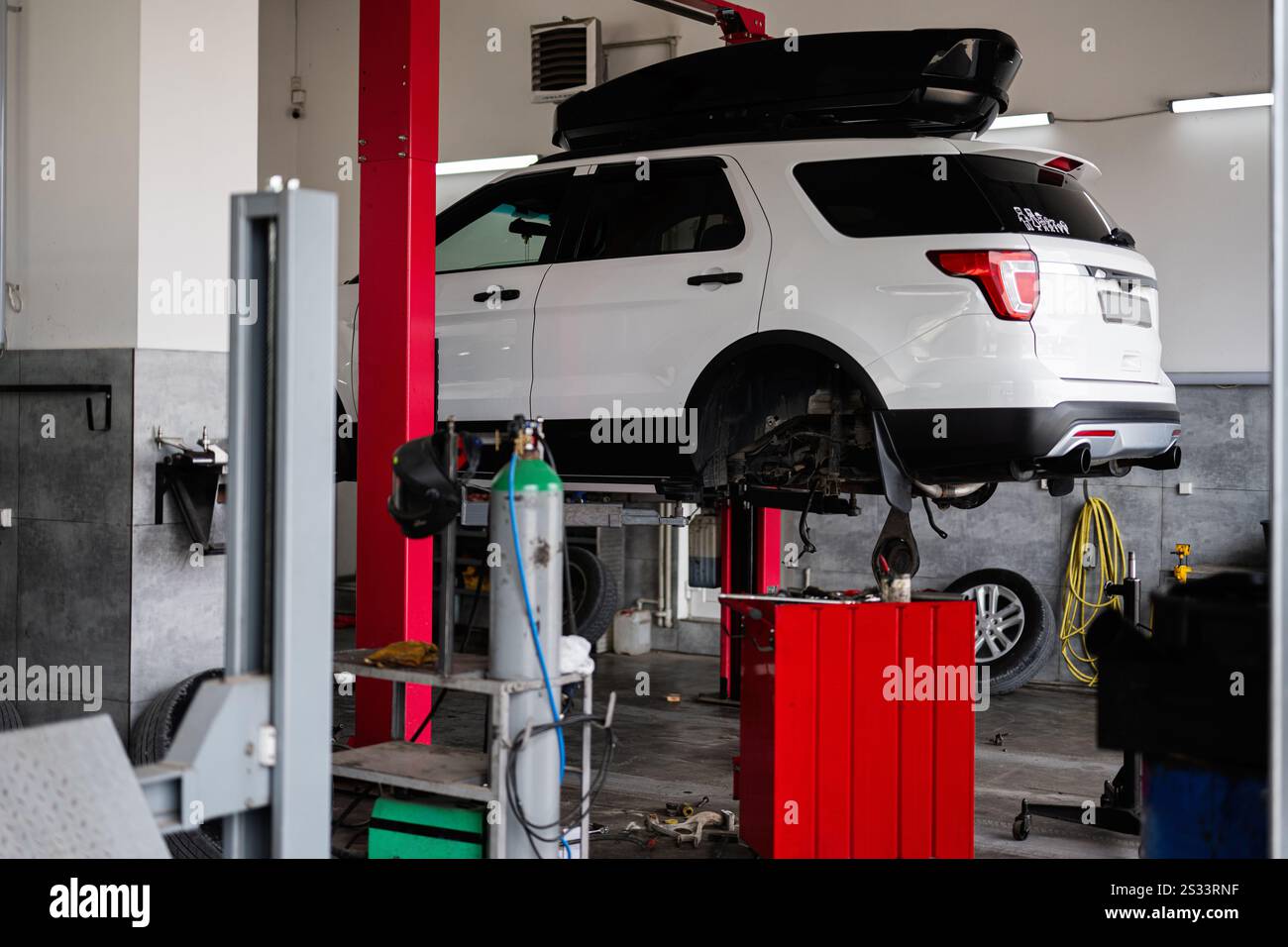 A white SUV is elevated on a hydraulic lift in an auto repair garage ...