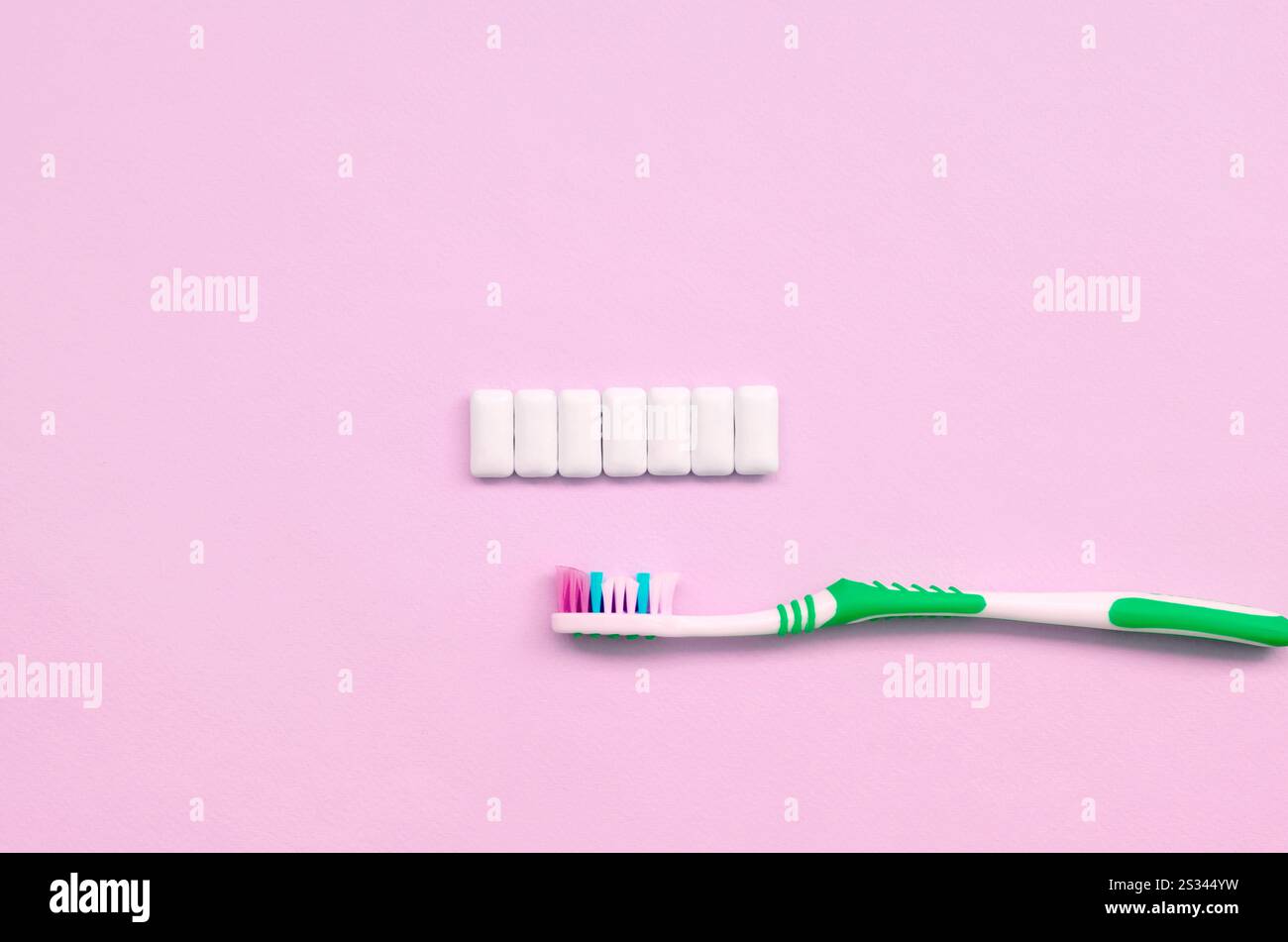 Toothbrush and chewing gums lie on a pastel pink background. Top view ...