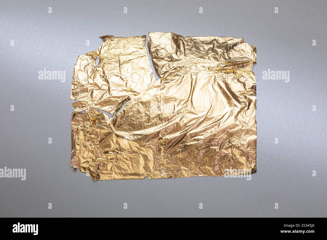 Shiny and crumpled gold foil sheet on a smooth gray background with ...