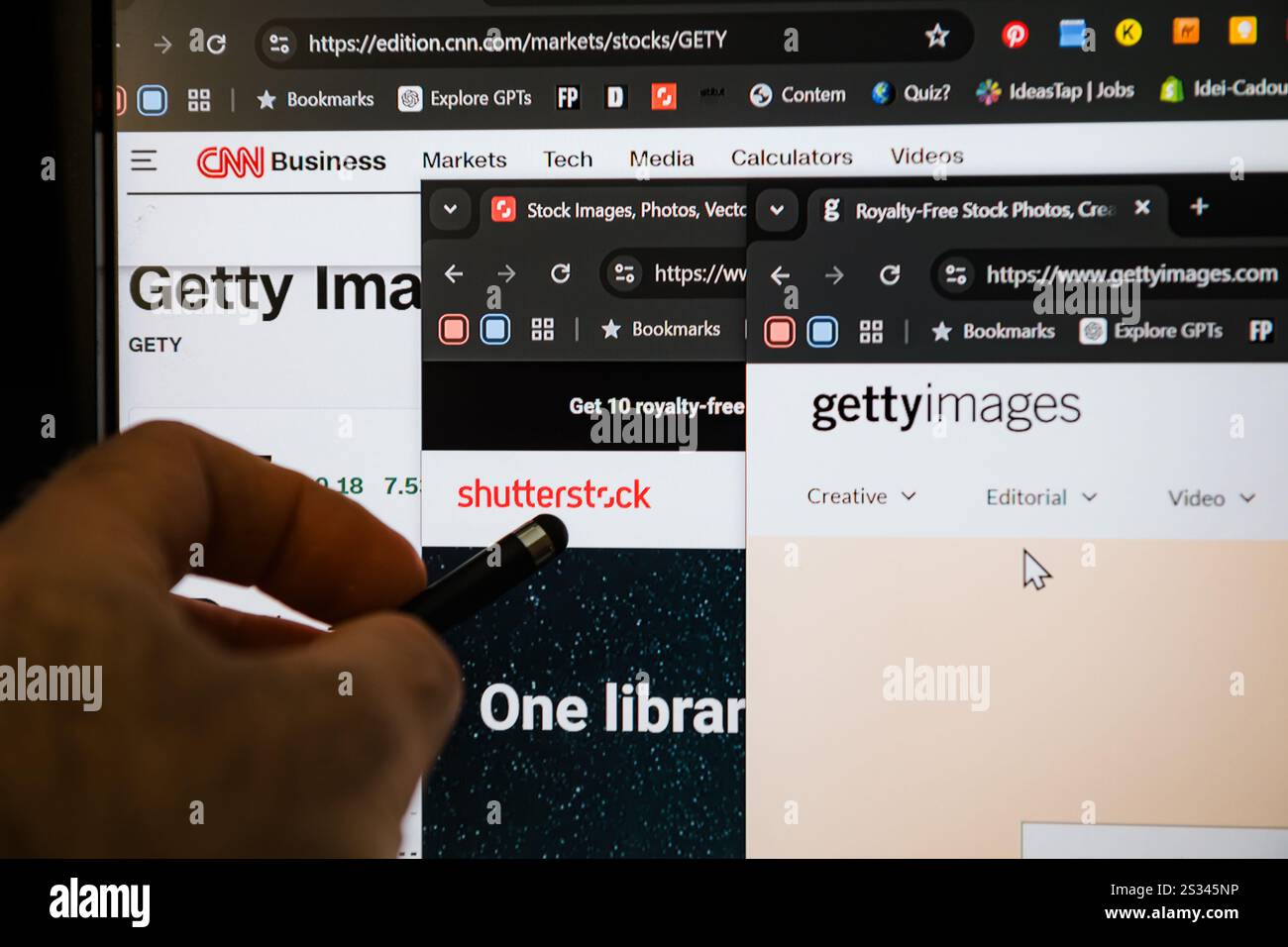 A hand pointing at a computer screen displaying open tabs for ...