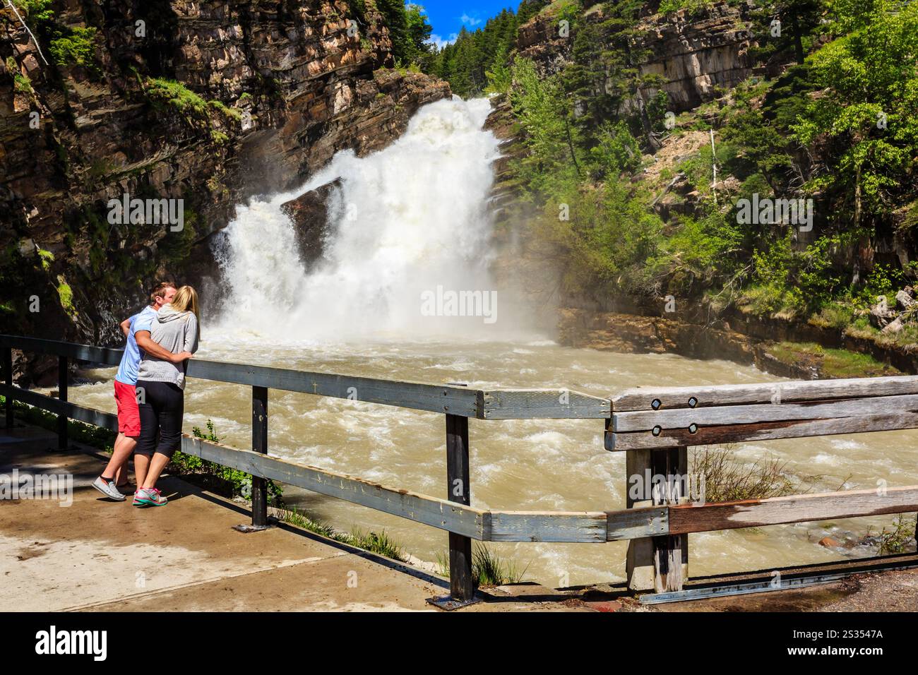 A couple is kissing in front of a waterfall. The water is flowing over ...