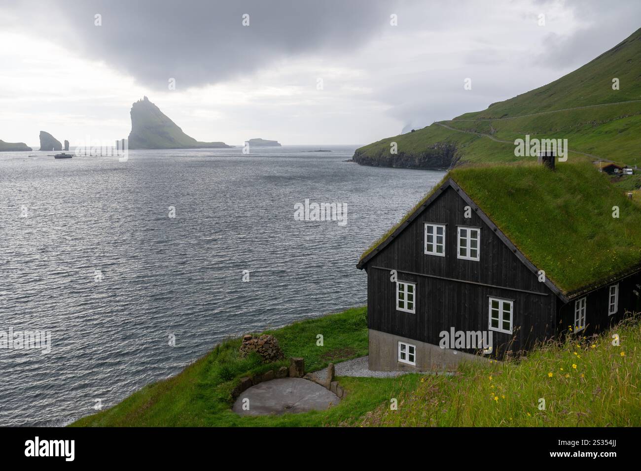 Traditional faroese grass-covered cottages in the village Bour. Drangarnir and Tindholmur sea ...
