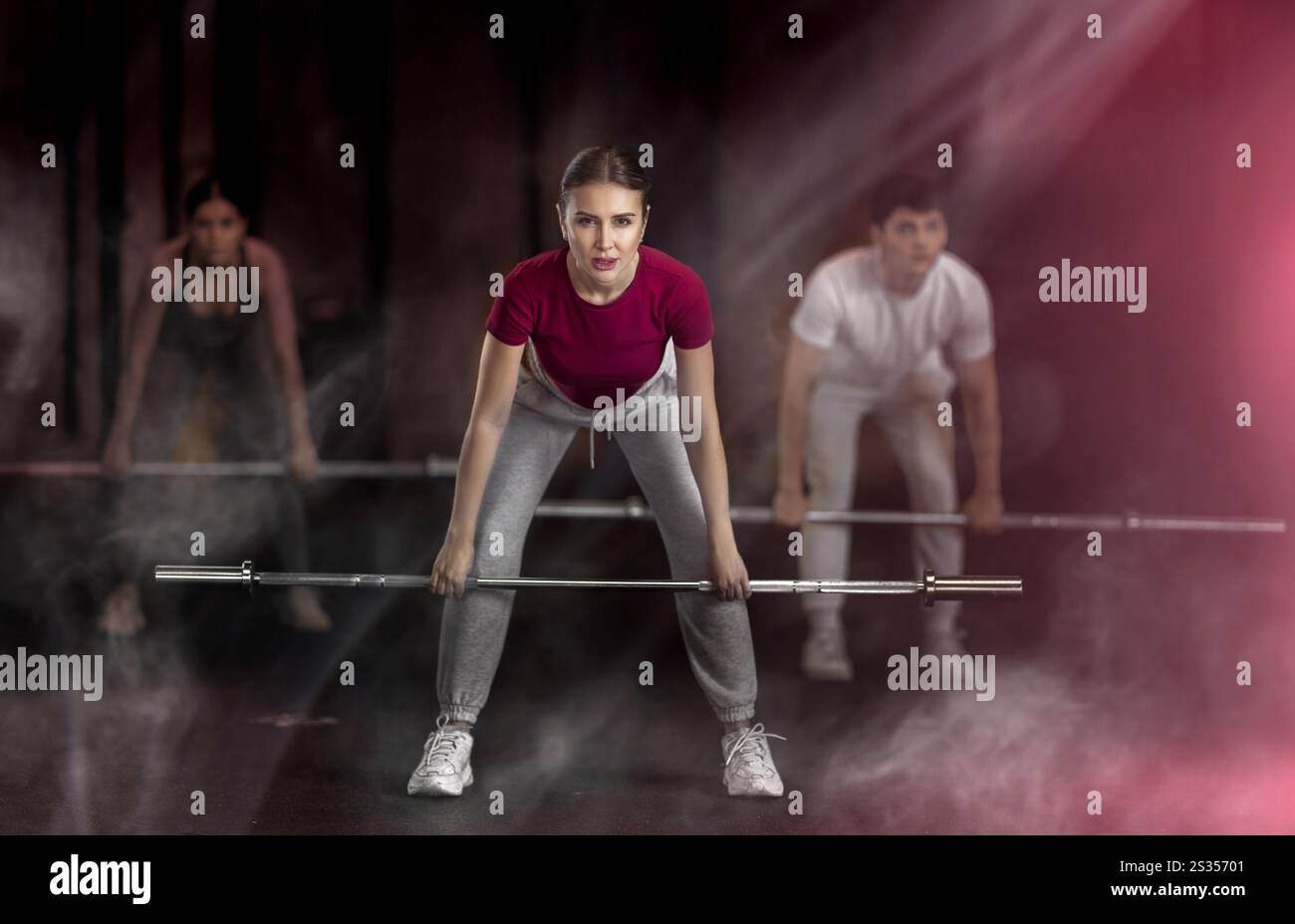 Slender girl trains muscles of arms and back using barbell and ...