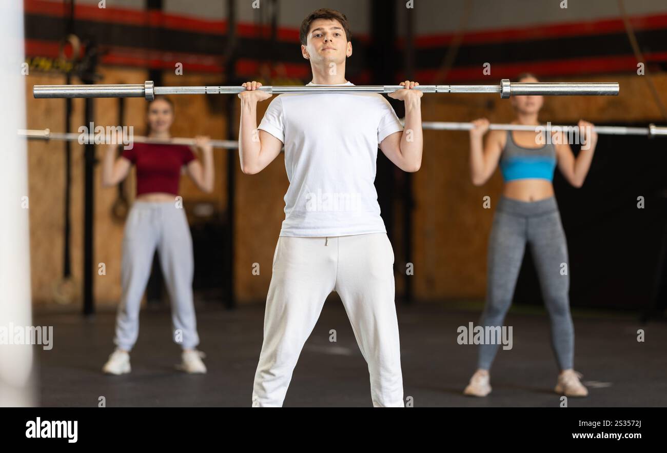 Slender guy trains muscles of arms and back using barbell and ...