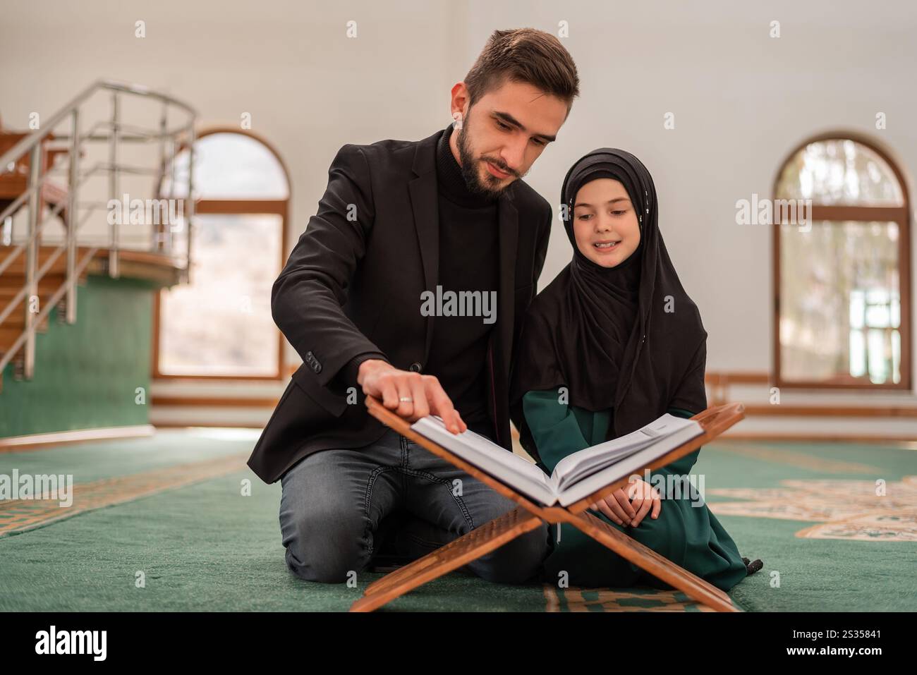A Muslim teacher teaching child girl to reading a holy book Quran inside the Mosque Islamic ...