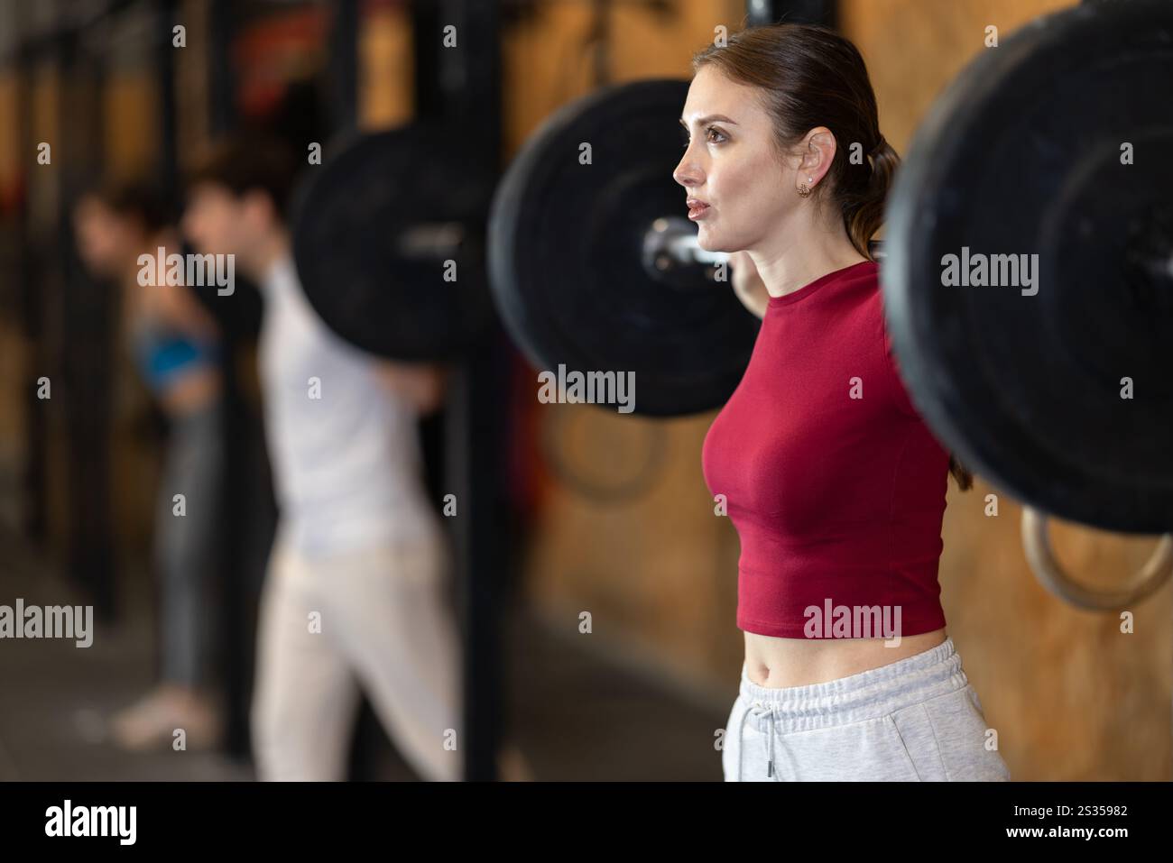 Slender girl trains muscles of arms and back using barbell and ...