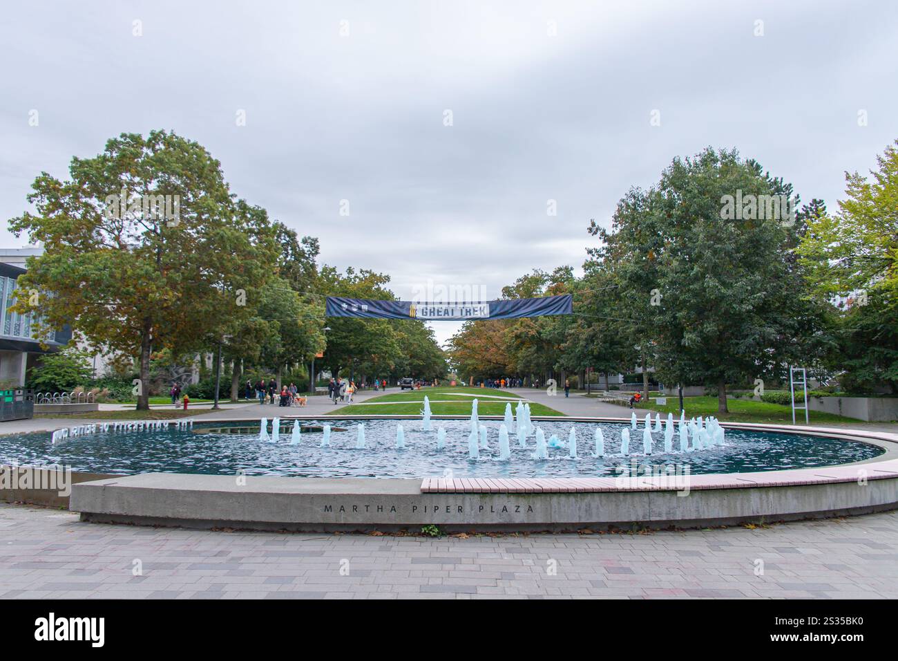 Fountain at Martha Piper Plaza on the UBC campus, with autumn foliage with students walking ...