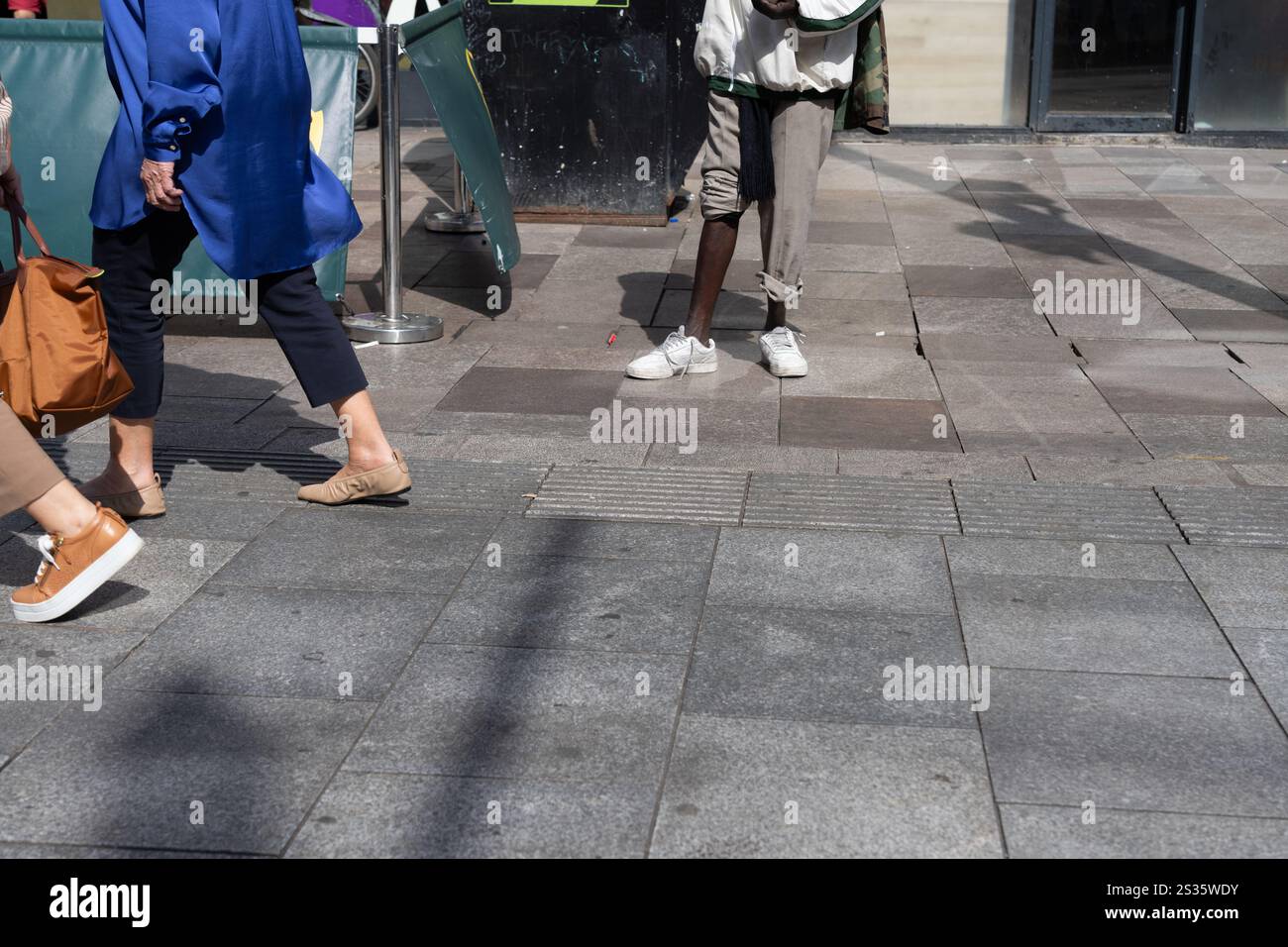 City footpath with woman’s legs and feet leaving frame with patterned ...