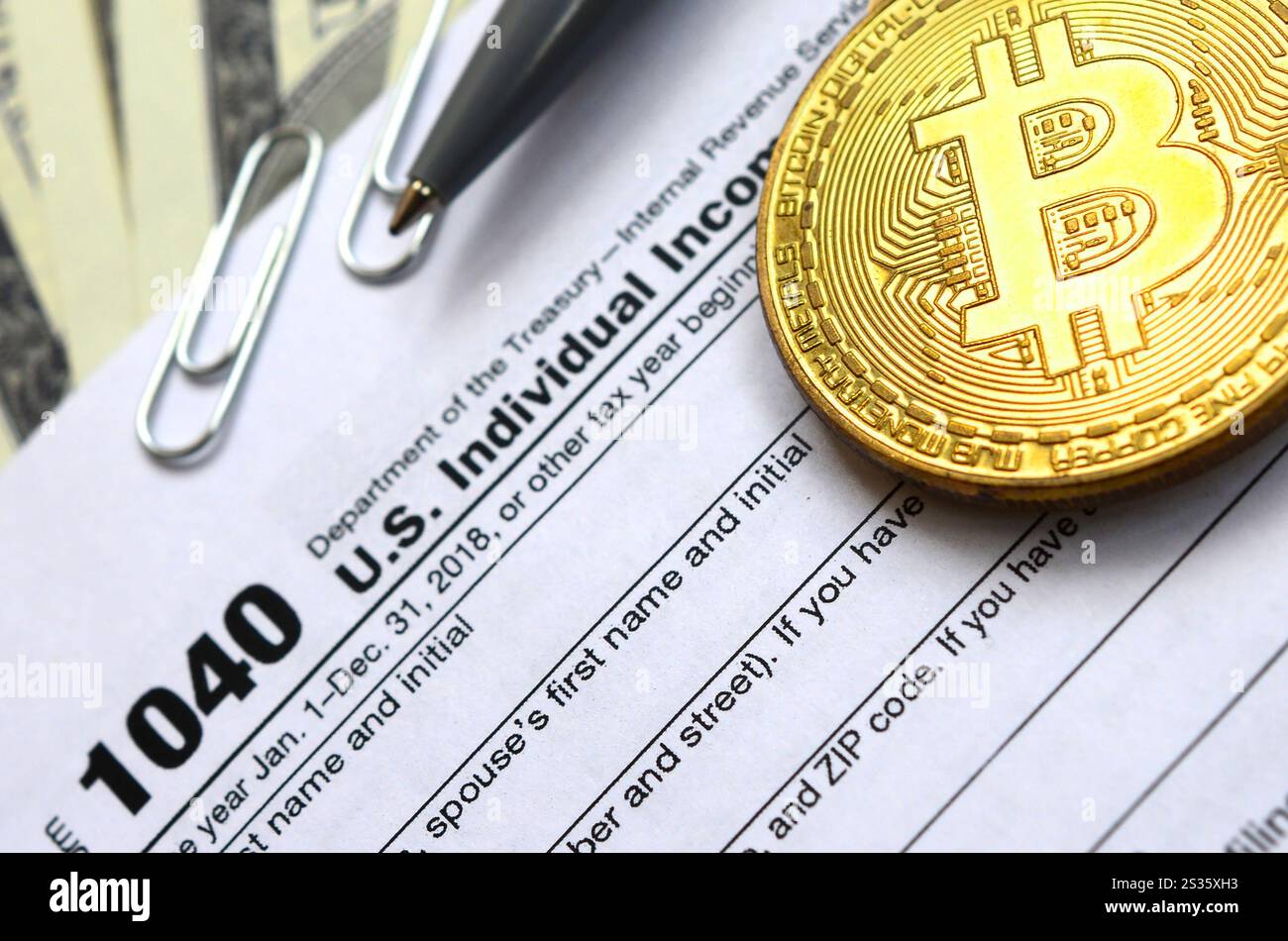 The pen, bitcoins and dollar bills is lies on the tax form 1040 U.S ...