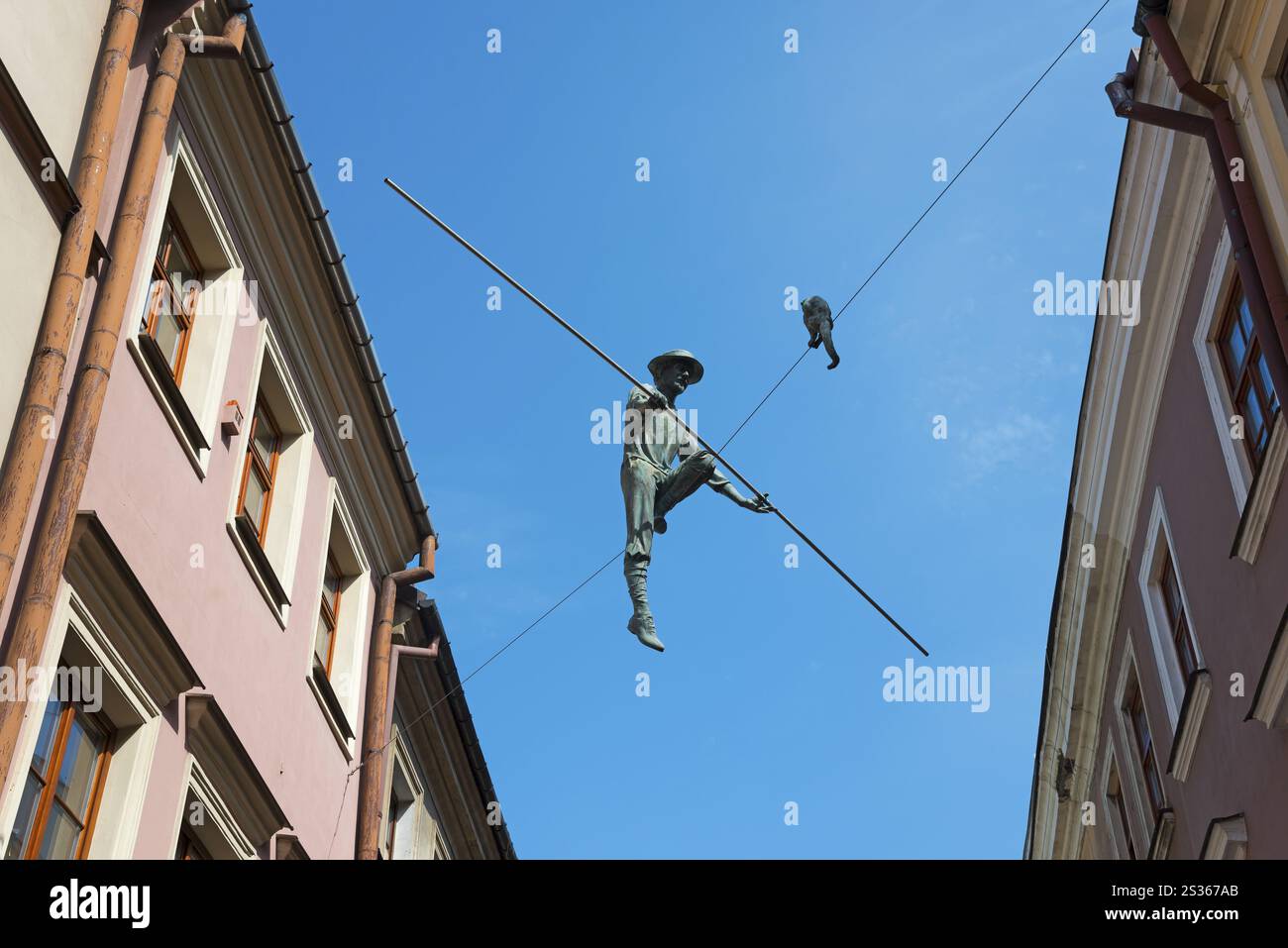 Tightrope walker statue balancing between buildings under blue sky, tightrope walker and monkey ...