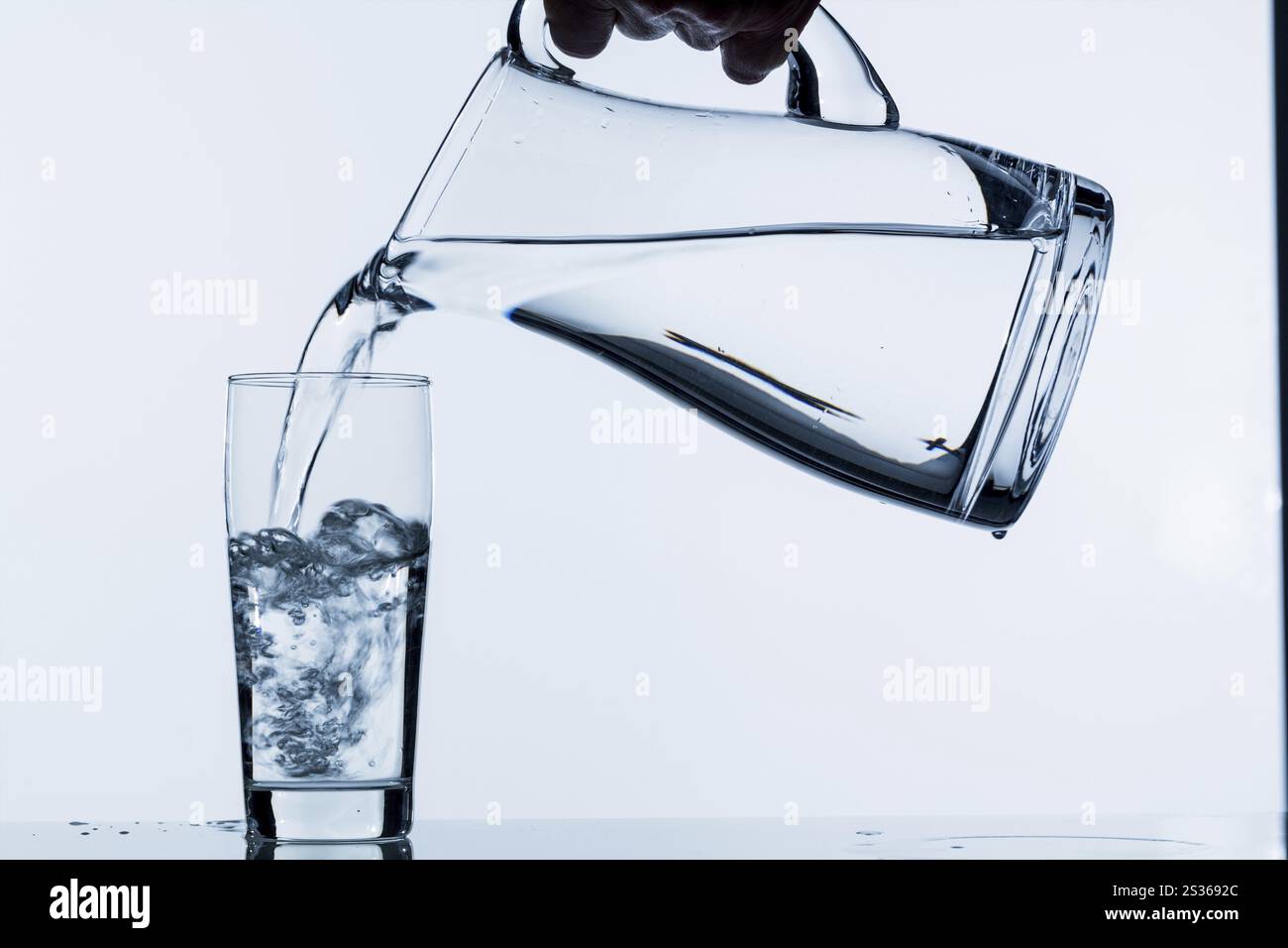 Pure water is poured into a water glass from a jug. Fresh drinking ...
