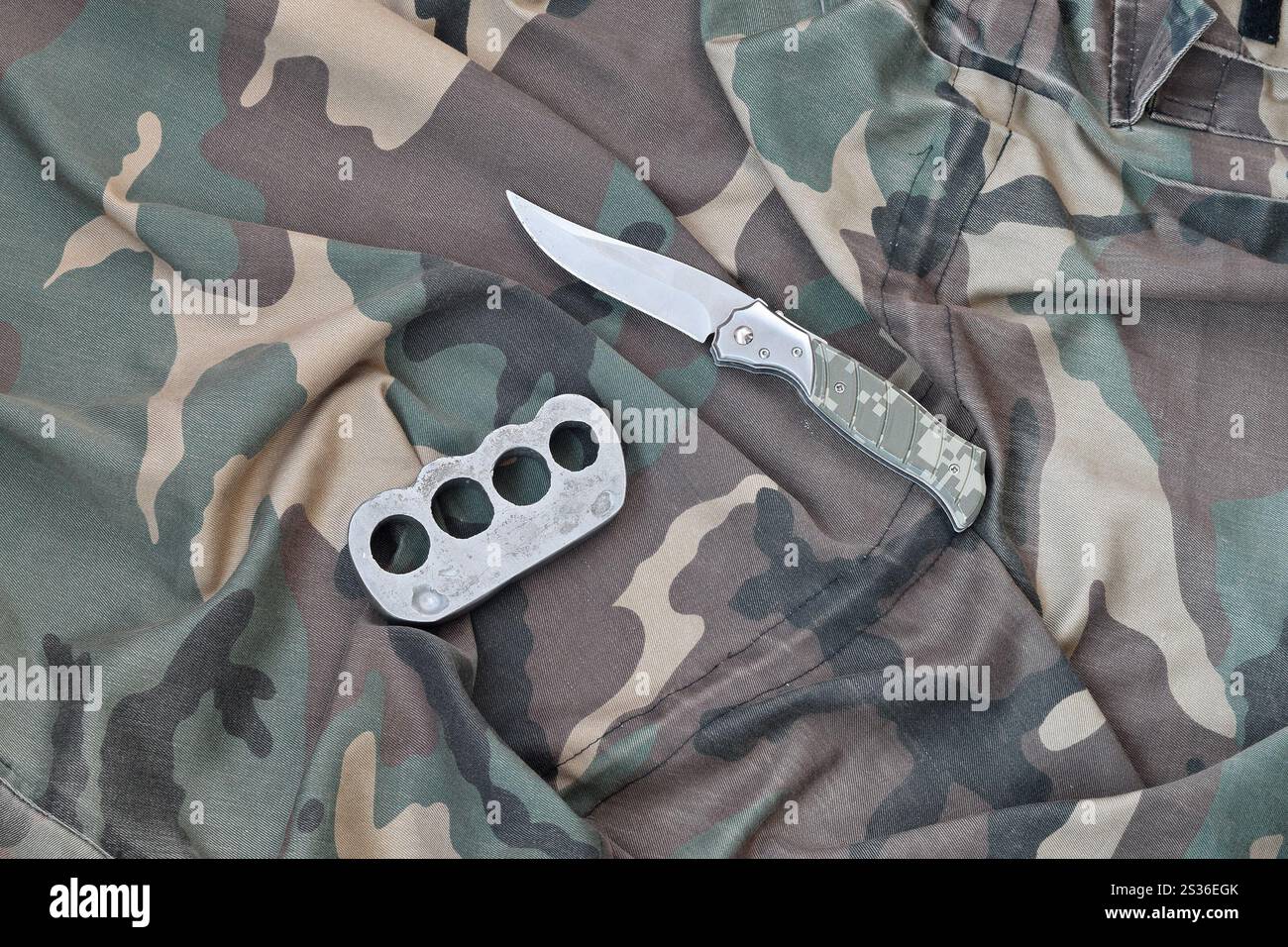 Knife and brass knuckles on a camouflage clothes background. Tools for ...