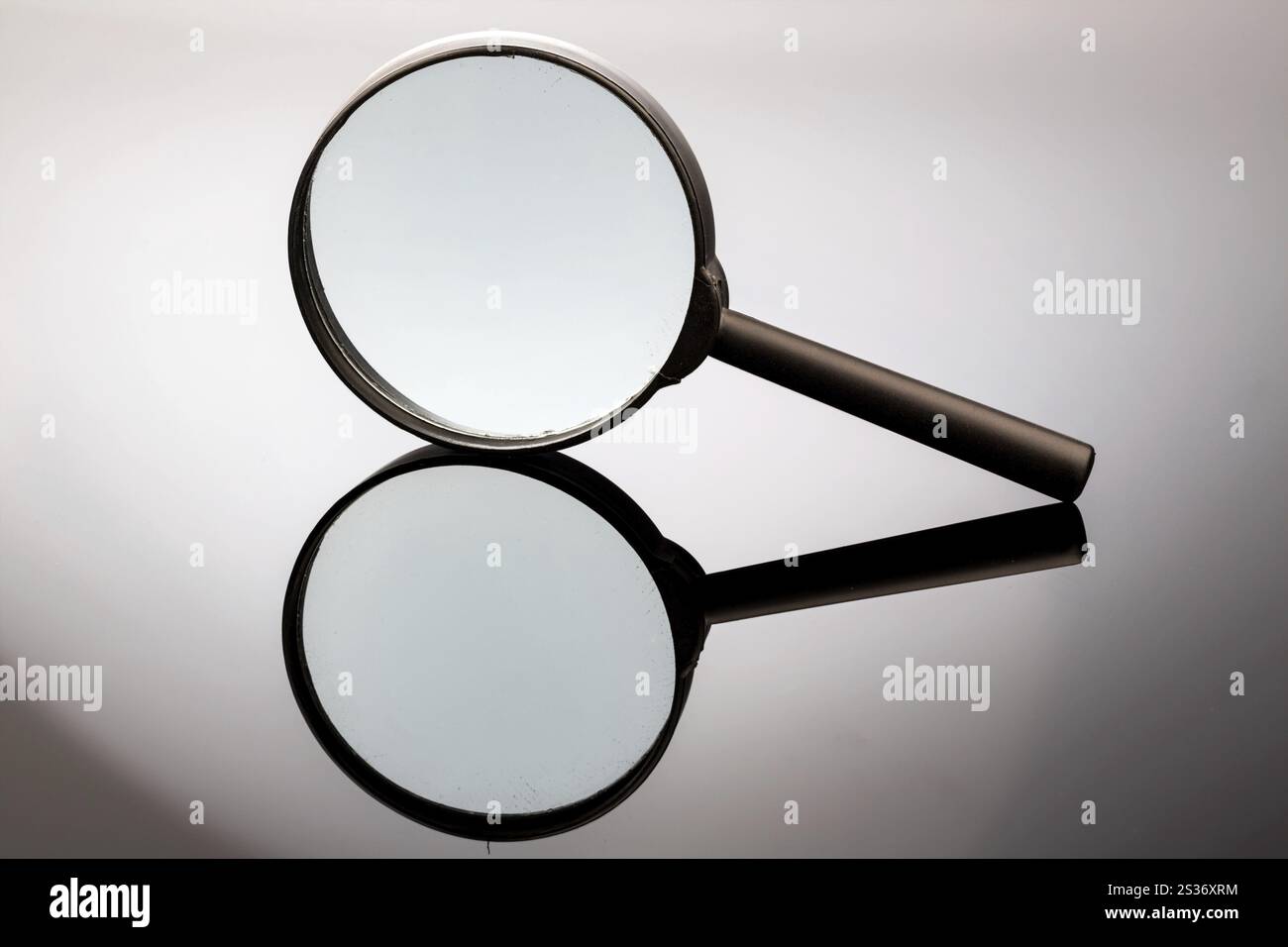 A magnifying glass lies on a grey background and is reflected Stock ...