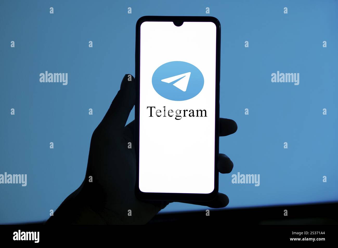 The TELEGRAM app logo on the screen of a cell phone that a man is ...