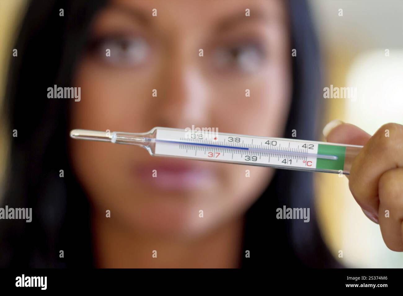 A woman holds a clinical thermometer behind her hand. Symbol photo for sick and fever Austria ...
