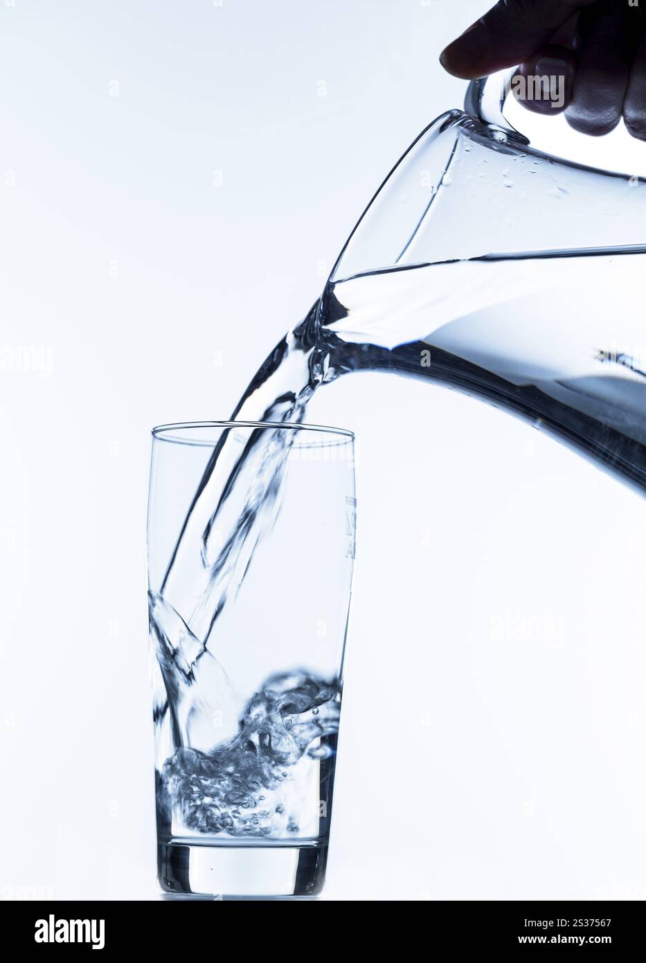 Pure water is poured into a water glass from a jug. Fresh drinking ...