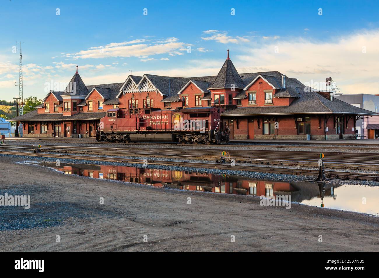 A train is parked in front of a large brick building. The train is red ...